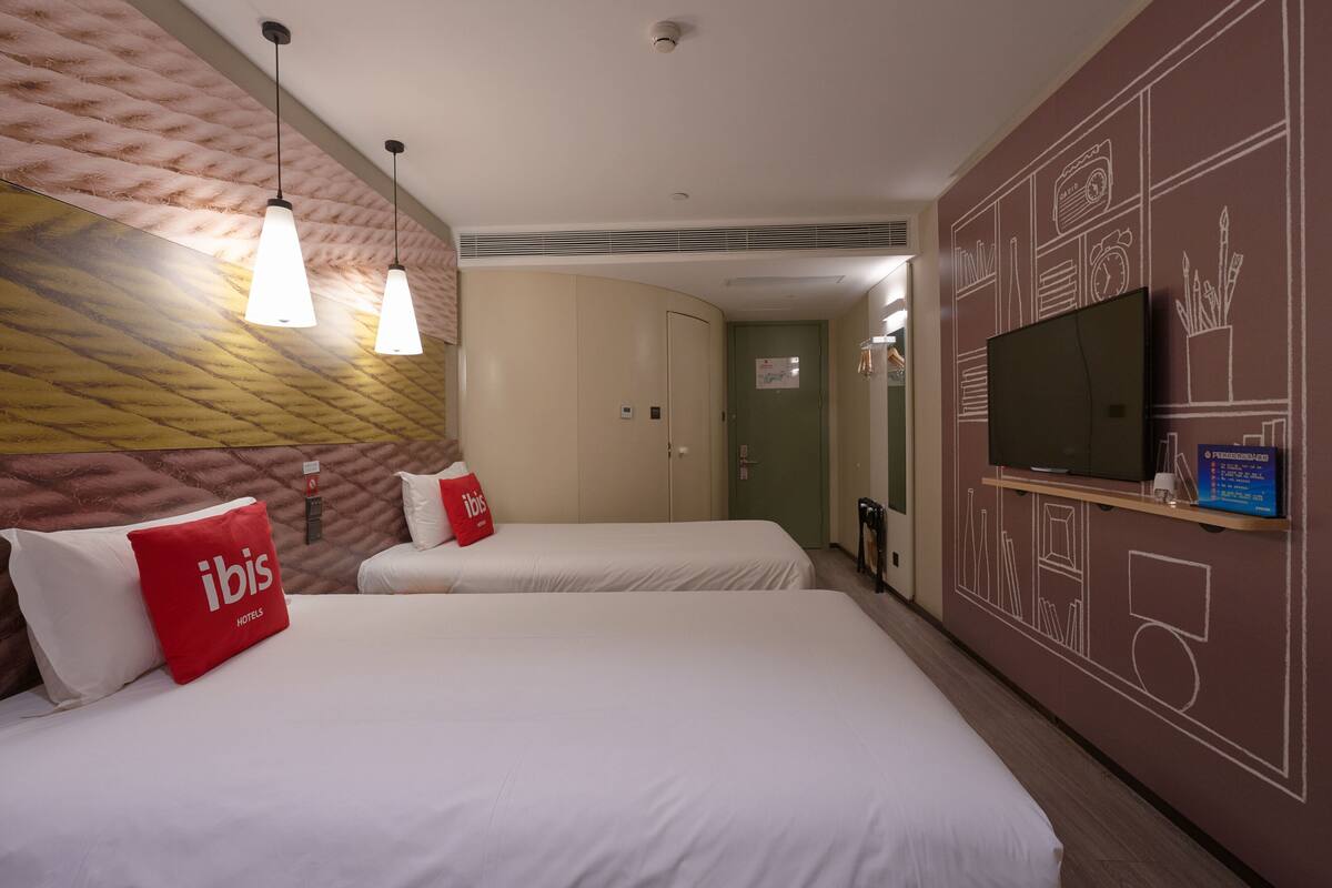 Quarto de hotel com duas camas, uma televisão e um minibar.