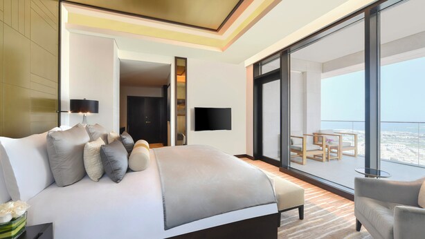 Quarto de hotel moderno com uma cama grande, televisão de tela plana, varanda com vista e área de estar separada.