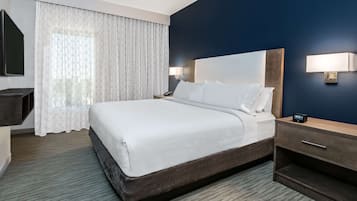 Quarto de hotel com uma cama grande, mesa de cabeceira, escrivaninha, televisão e janela com cortinas.