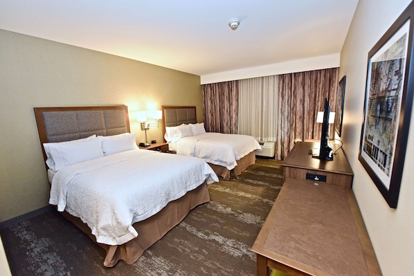 Quarto de hotel com duas camas, uma mesa, uma luminária e um quadro na parede.