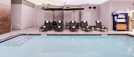 Uma área de piscina com espreguiçadeiras e guarda-sóis, uma piscina com azulejos azuis e um edifício com o número 221 na parede.