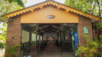 Um restaurante com fachada de madeira, entrada de vidro e mesas ao ar livre visíveis através das portas.