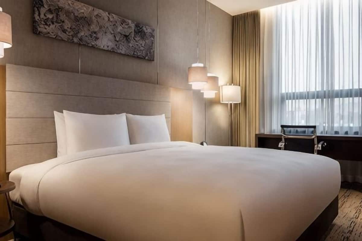 Uma cama grande com roupa de cama branca, cabeceira e mesa de cabeceira com abajur.