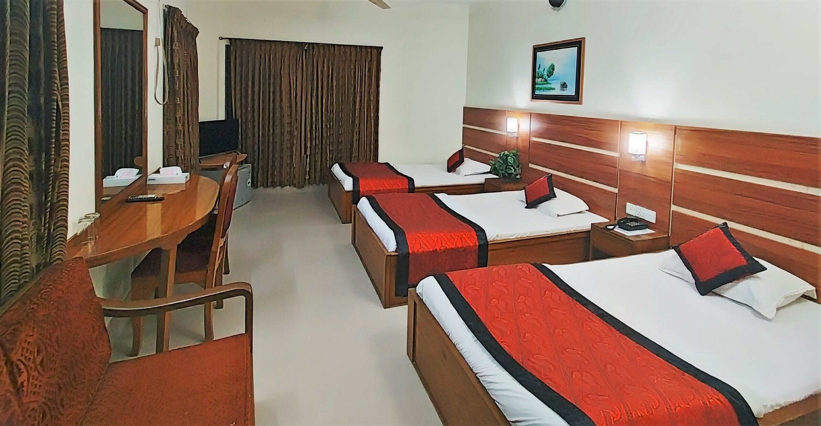 Quarto de hotel com três camas de solteiro, uma escrivaninha de madeira, uma cadeira, uma mesinha e um espelho.