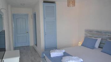 Quarto com cama, duas portas azuis, mesa de cabeceira e criado-mudo.