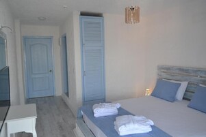 Quarto com cama, duas portas azuis, mesa de cabeceira e criado-mudo.