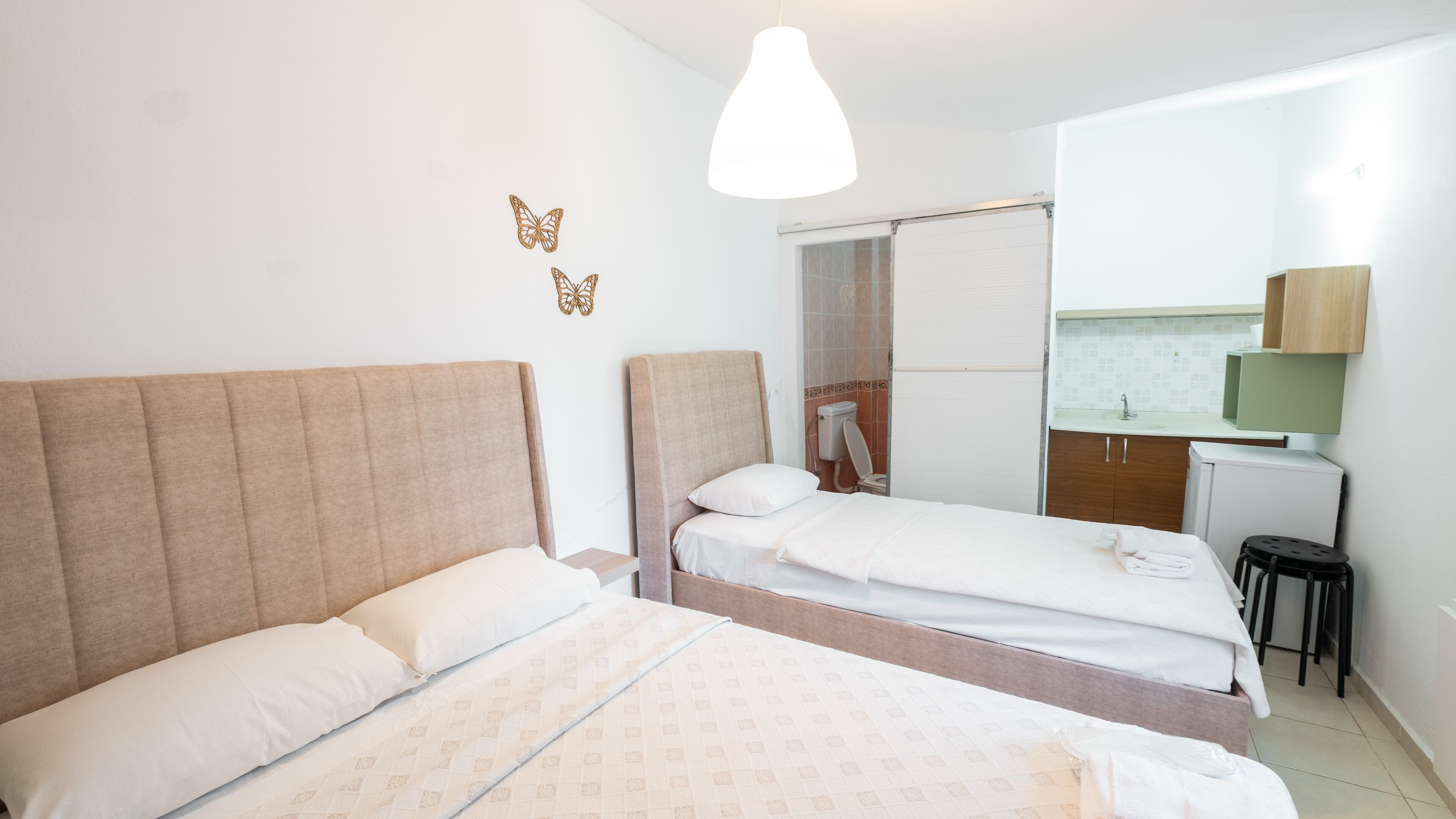 Quarto de hotel com duas camas, uma cozinha compacta e área de chuveiro.