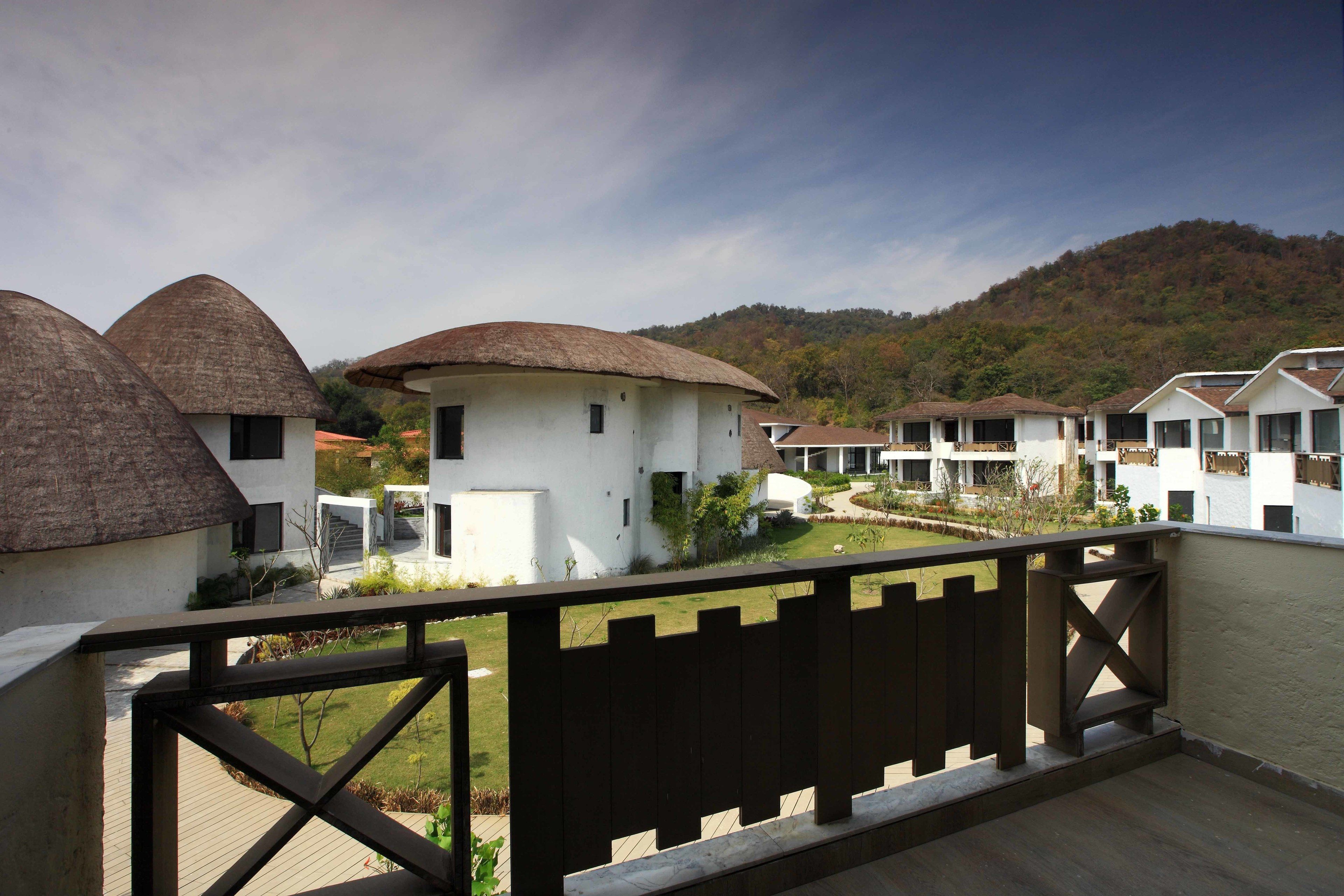Um resort com chalés de telhado de palha, um deck de madeira e vista para uma colina arborizada.