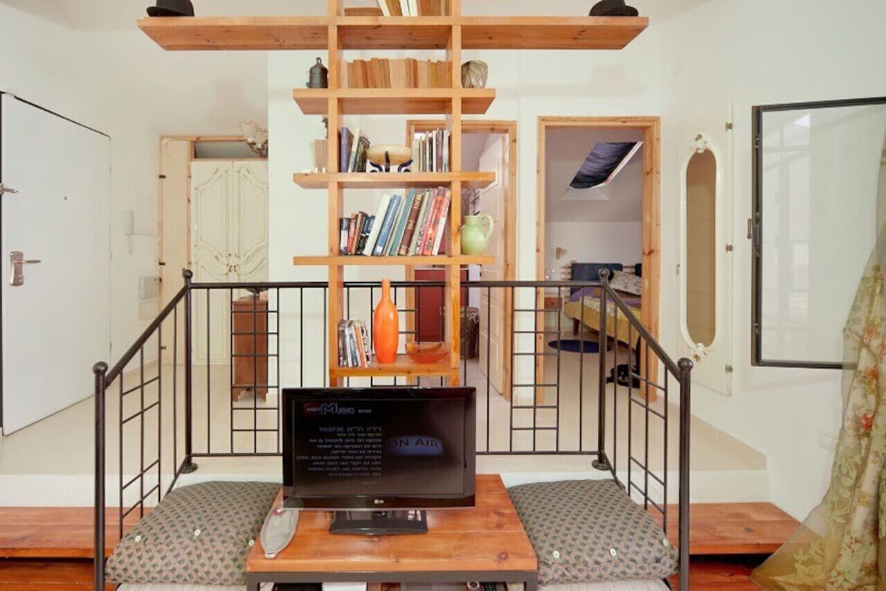 Quarto com uma estante de madeira, uma televisão de tela plana sobre uma mesa de madeira e uma escada com corrimão de metal.