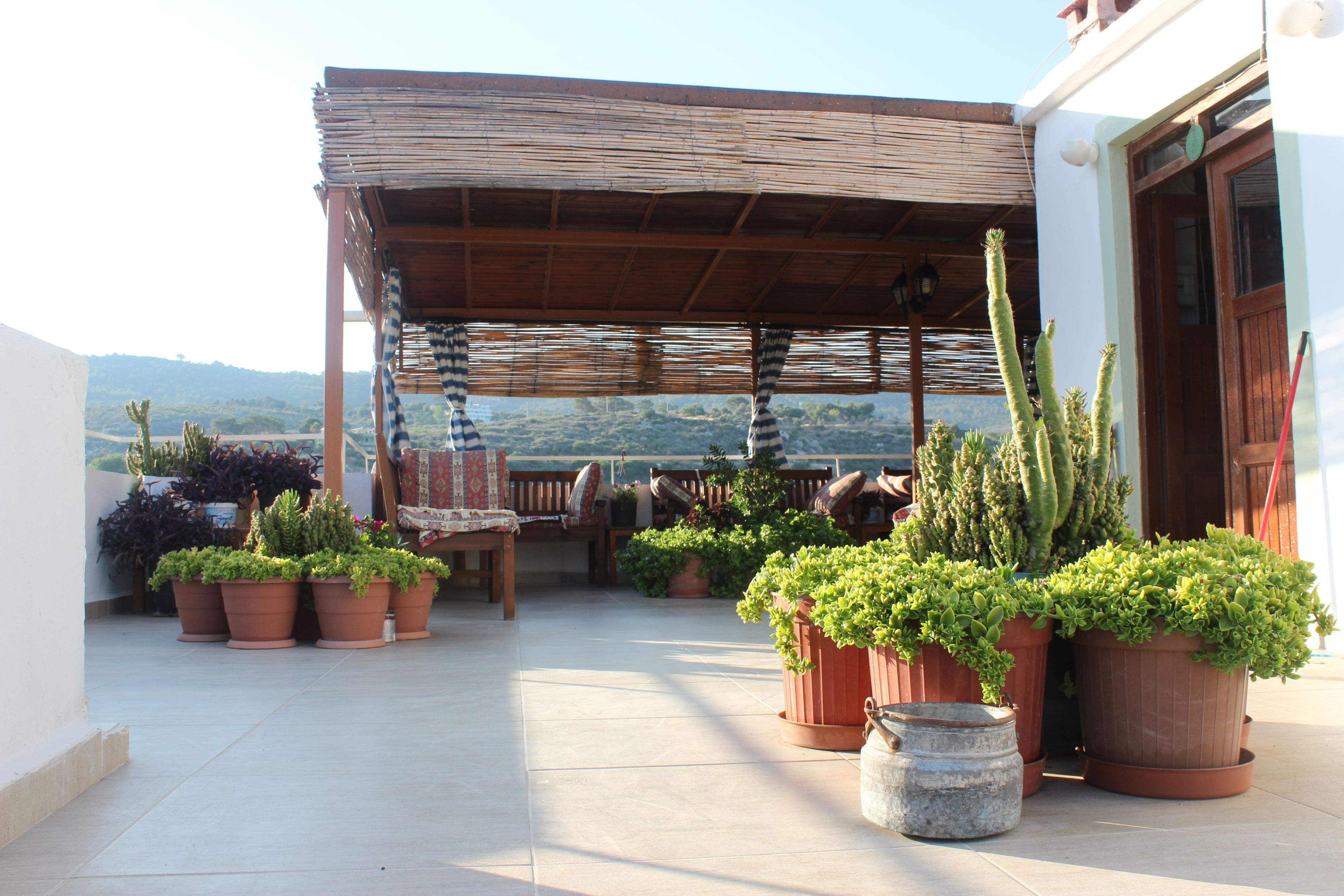 Uma área de estar coberta ao ar livre, com plantas em vasos e vista para as colinas.