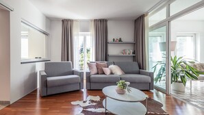 Uma sala de estar moderna com um sofá cinzento, uma mesa de centro redonda e uma porta de vidro que dá para uma varanda.