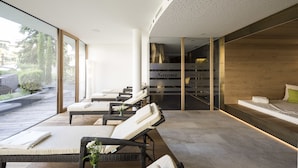 Uma área de spa moderna com espreguiçadeiras de vime, um balcão de recepção em madeira e uma parede de vidro que dá para uma sauna.