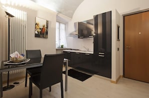 Cozinha compacta com área de jantar, apresentando fogão moderno, armários pretos e porta de madeira.
