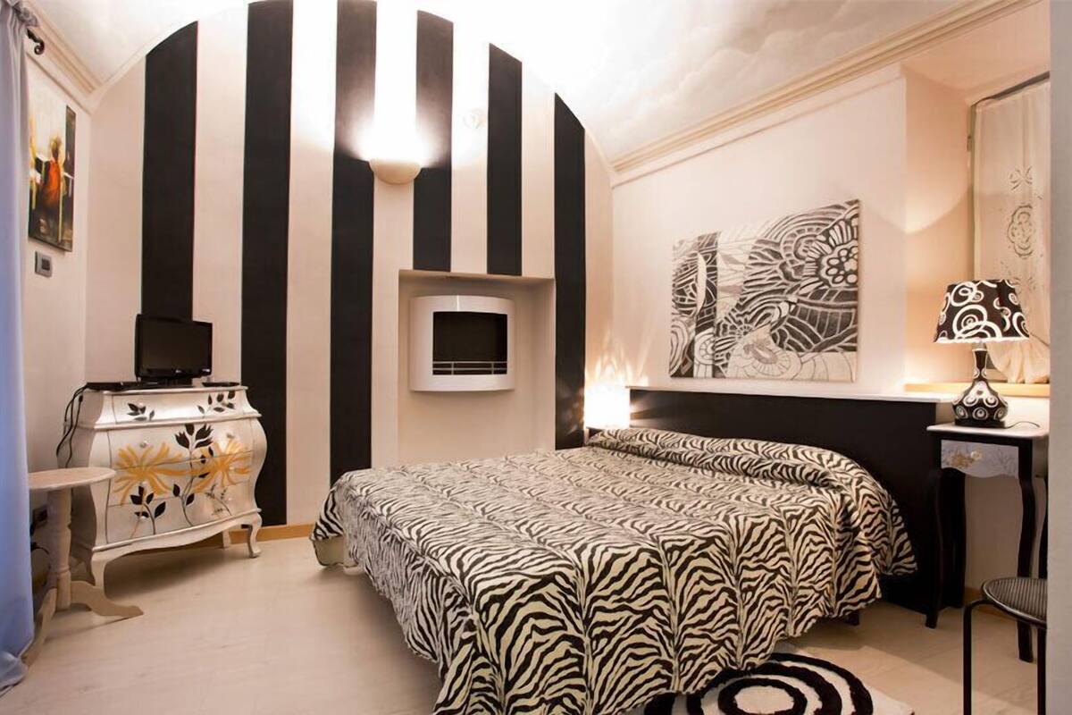 Quarto com cama estampada em padrão de zebra, escrivaninha com luminária, televisão e um objeto decorativo na parede.
