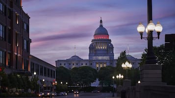 Um grande edifício governamental com uma cúpula imponente, rodeado por árvores e postes de luz.