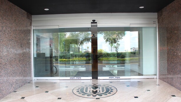Uma entrada moderna com porta de vidro, logotipo no chão e vista para o exterior.