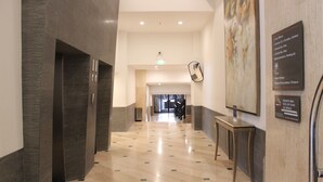 Um hall de hotel moderno com piso de mármore, um balcão de recepção e uma escadaria que leva aos andares superiores.