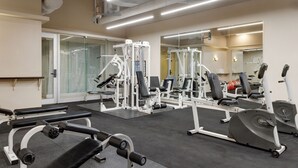 Uma academia com diversos equipamentos de exercícios, bancos e um espelho grande na parede.