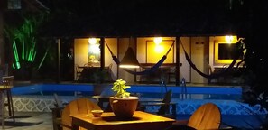 Área de piscina com mesa, cadeiras e uma rede.