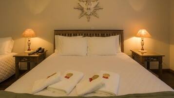 Quarto de hotel com uma cama grande, duas mesas de cabeceira com abajures, e um objeto decorativo acima da cama.
