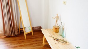 Quarto com piso de madeira, um cavalete, um manequim de madeira, uma mesa com um vaso e uma garrafa.