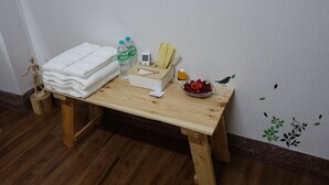 Uma mesa de madeira com toalhas, garrafas de água, uma caixa de lenços, uma pequena tigela de flores secas e uma figura de madeira.