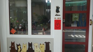 Fachada com porta vermelha, janela refletindo uma bicicleta e um mural de cães na parede.