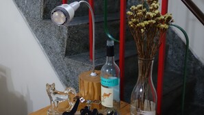 Uma mesa de madeira com uma garrafa de licor, um vaso com flores secas e uma estatueta de gato.