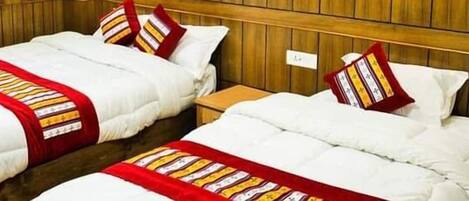 Duas camas de solteiro com roupa de cama branca e cobertores listrados em vermelho e amarelo, cabeceiras de madeira e uma pequena mesa de cabeceira de madeira entre elas.