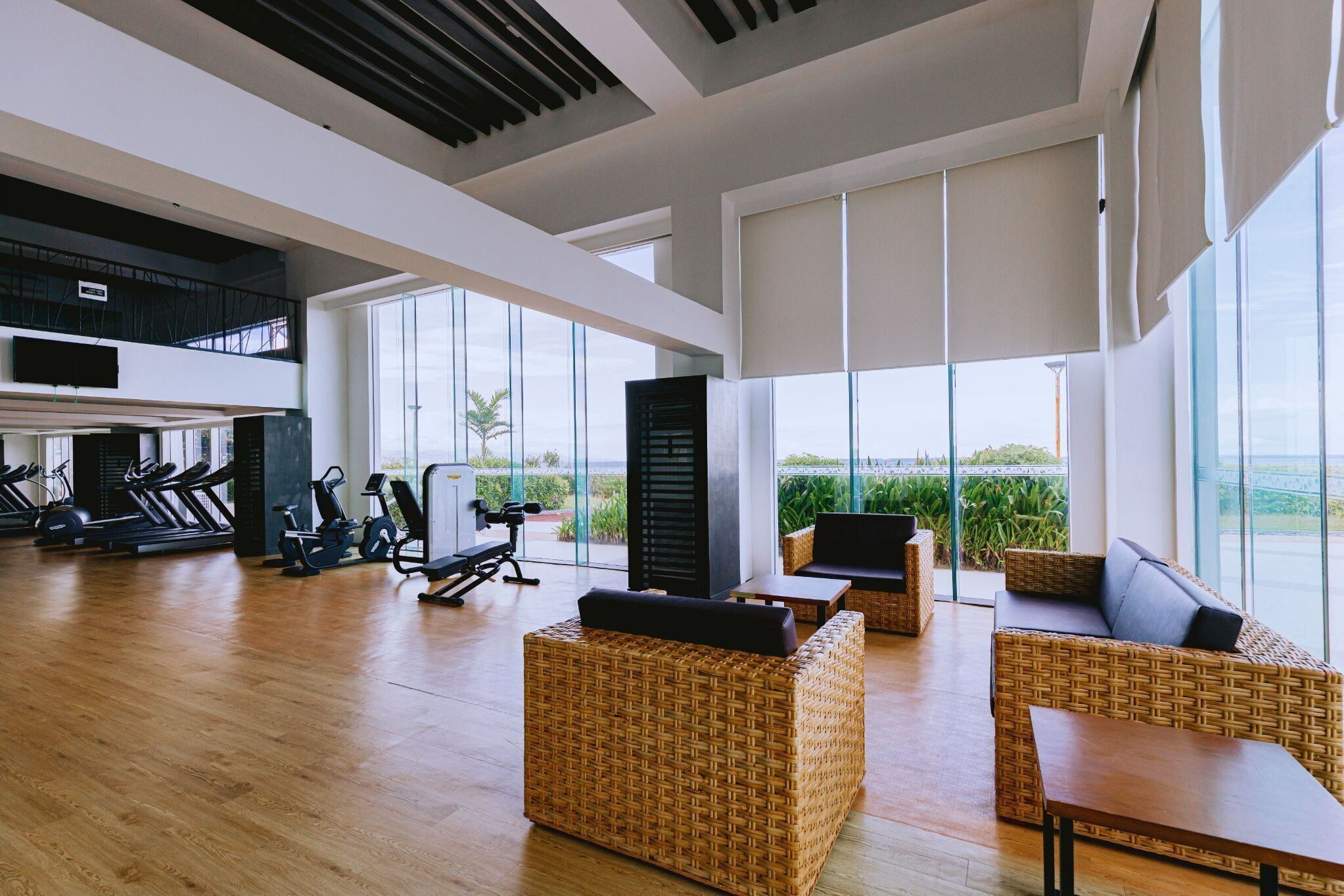 Uma academia ampla com equipamentos de ginástica e grandes janelas com vista para o exterior.