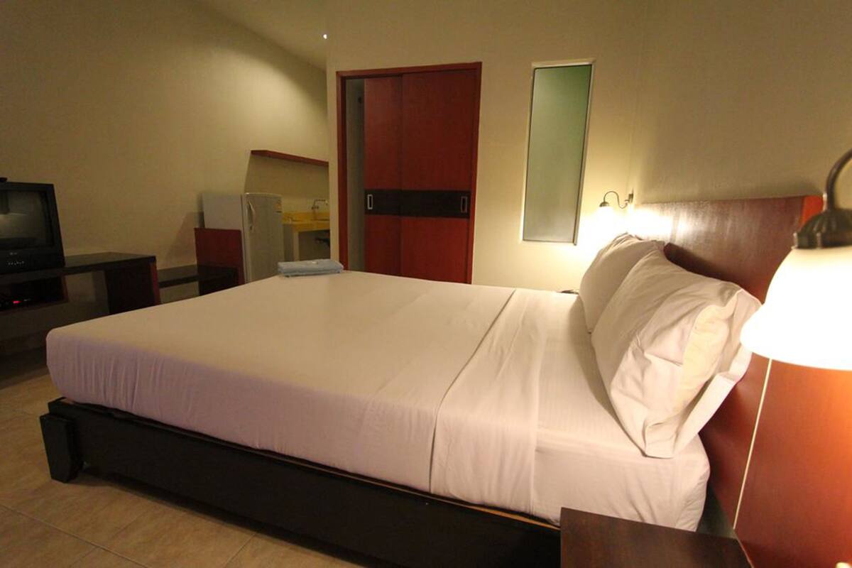 Quarto de hotel com cama, televisão, guarda-roupa e espelho.