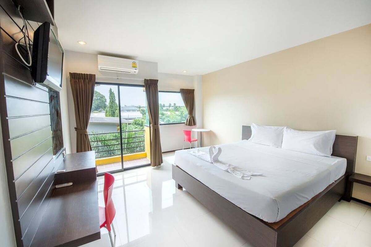 Quarto de hotel com cama, escrivaninha, cadeira, televisão e varanda com cortinas.