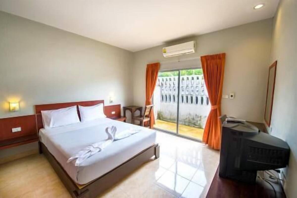Quarto de hotel com cama, televisão, escrivaninha e porta de vidro deslizante para área externa.