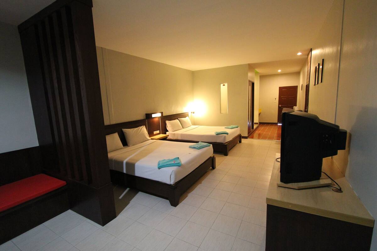 Quarto de hotel com duas camas, uma televisão e um banco vermelho.