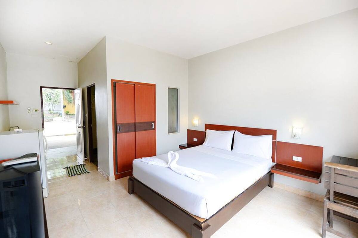 Quarto de hotel com uma cama grande, guarda-roupa de madeira, mesas de cabeceira e uma escrivaninha.