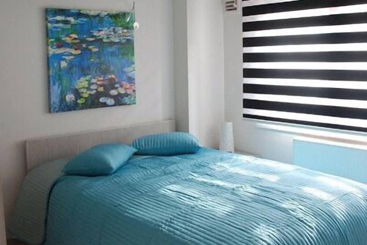 Um quarto com uma cama, um quadro e uma janela com persianas.
