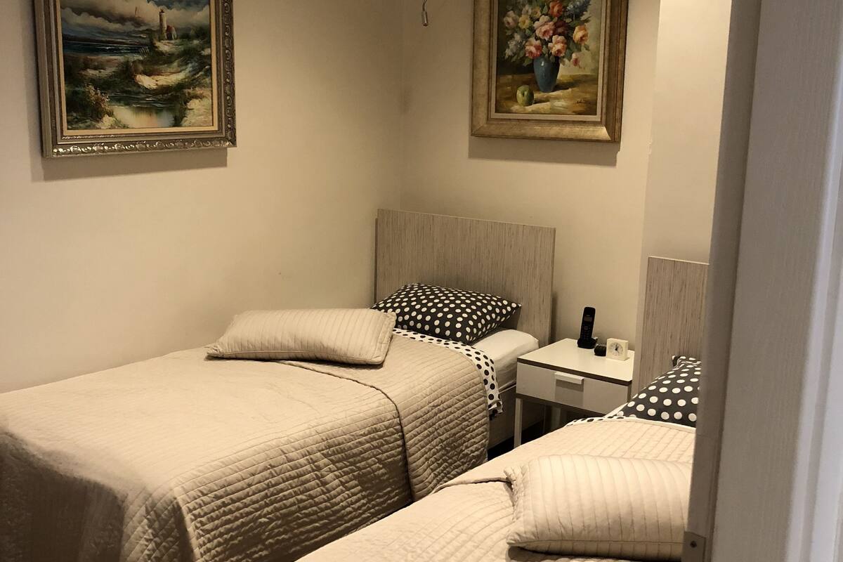 Quarto de hotel com duas camas, uma pequena escrivaninha e dois quadros na parede.