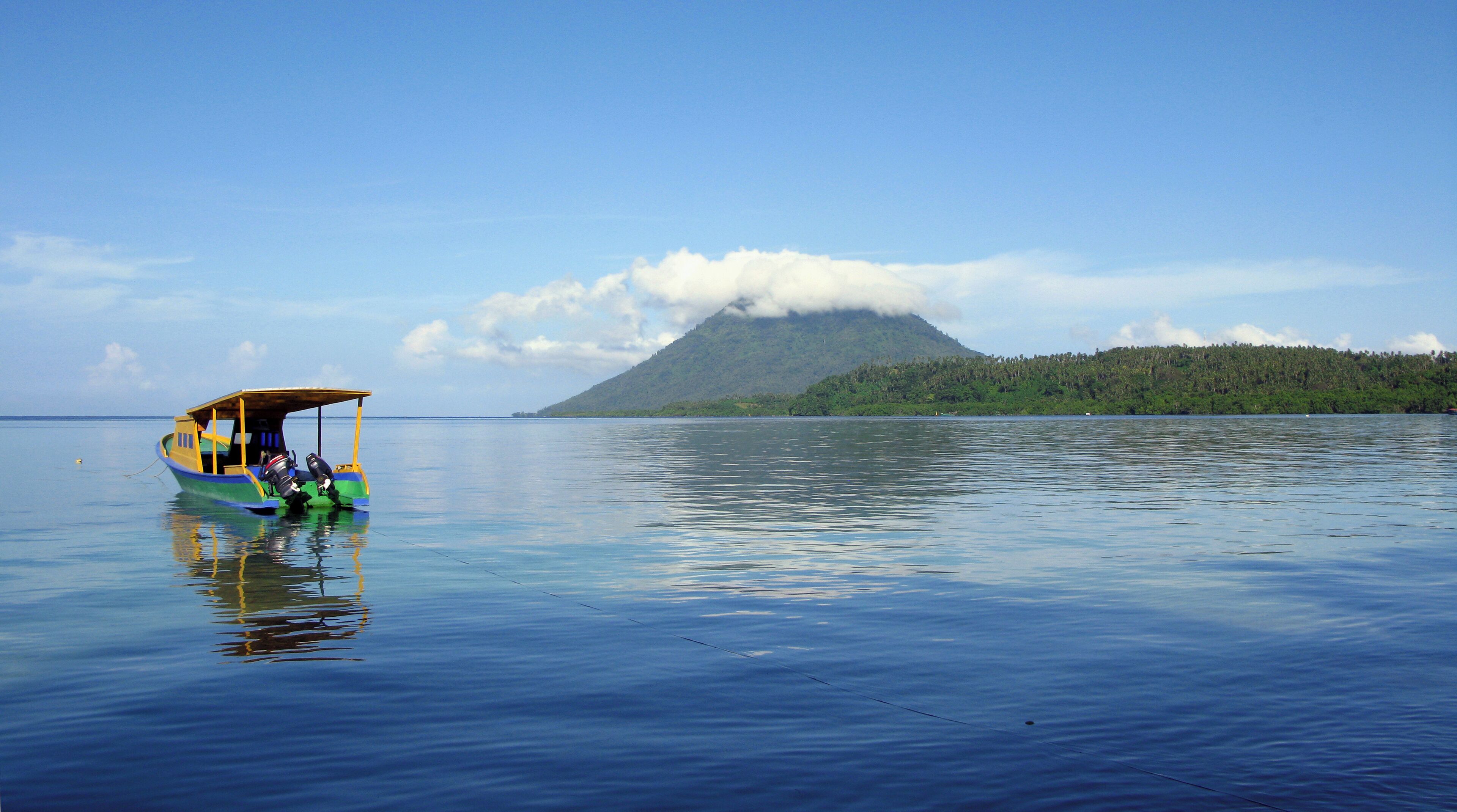 Um barco em águas calmas, com uma montanha e floresta ao fundo.