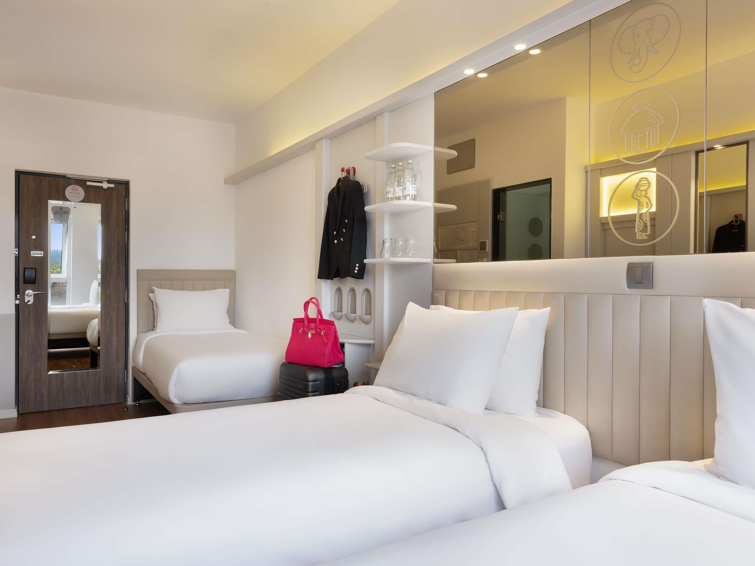 Quarto de hotel com duas camas, um espelho, um guarda-roupa e um banheiro visível por uma porta aberta.