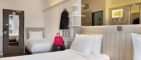 Quarto de hotel com duas camas, um espelho, um guarda-roupa e um banheiro visível por uma porta aberta.