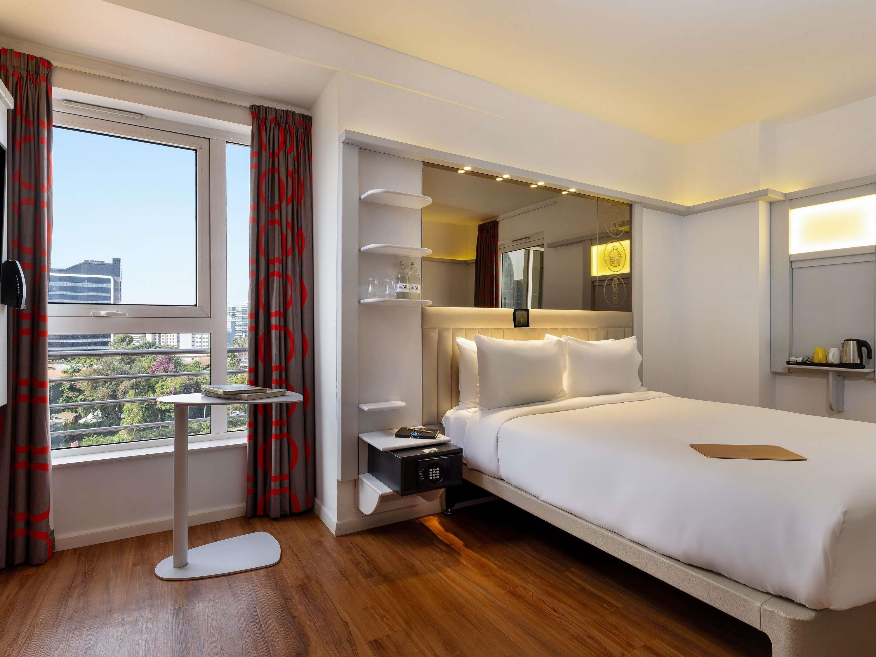 Quarto de hotel com uma cama grande, mesas de cabeceira, uma pequena mesa redonda, micro-ondas e vista para a cidade pela janela.