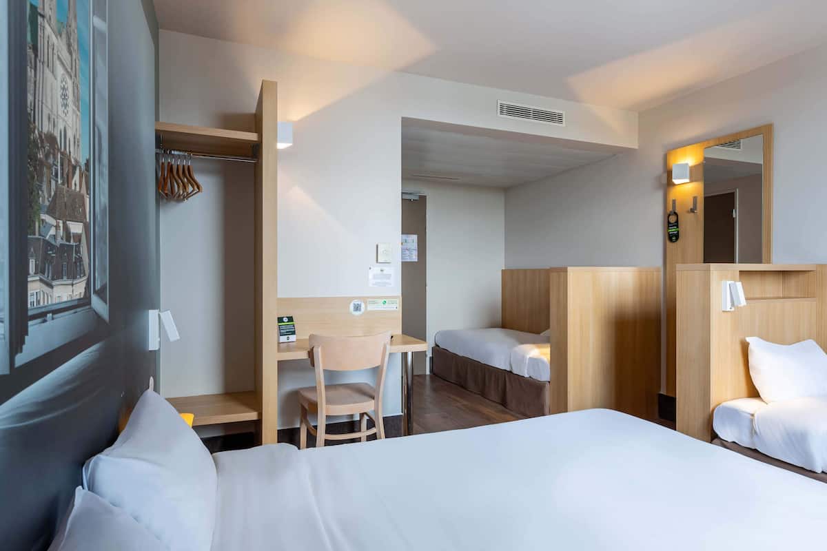 Quarto de hotel com duas camas, uma escrivaninha, uma cadeira e um guarda-roupa.
