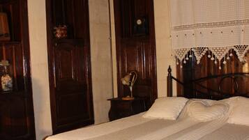 Quarto tradicional com cama de madeira, mesa de cabeceira e relógio de parede.