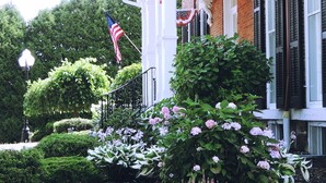 Um edifício de tijolos com varanda branca, bandeiras americanas e jardins bem cuidados.