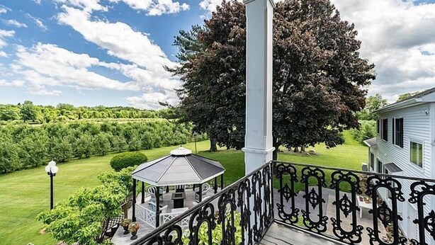 Varanda coberta com um gazebo, uma árvore grande e vista para uma paisagem verde.