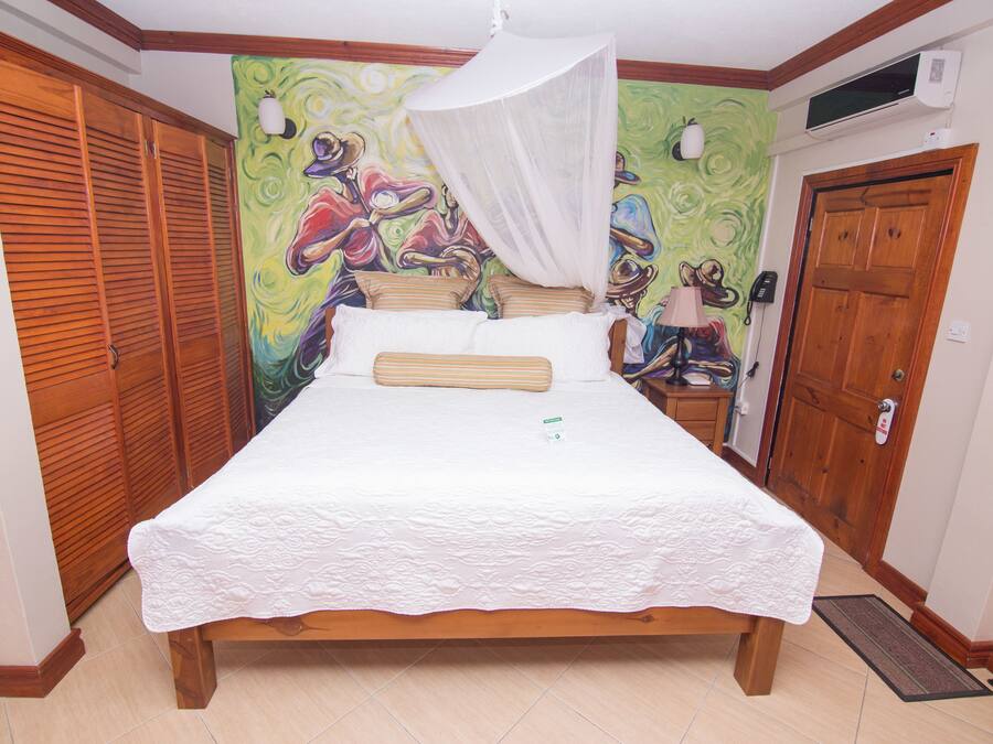 Um quarto com cama, guarda-roupa de madeira, parede com um mural colorido e uma porta com puxador.