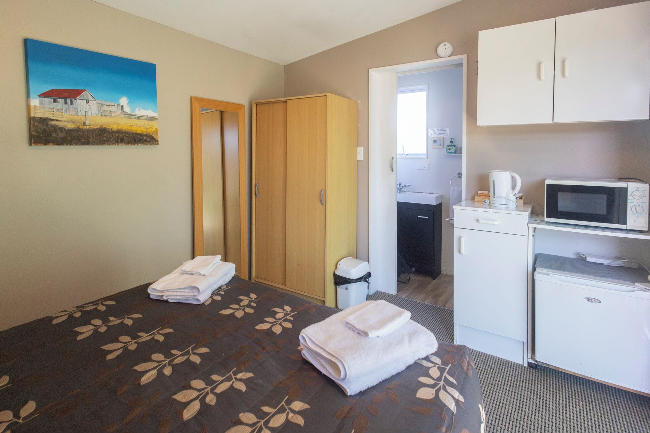 Quarto de hotel com cama, guarda-roupa, cozinha compacta e um quadro na parede.