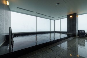 Uma grande piscina interior com paredes de vidro transparente, chão em mosaico e borda preta.