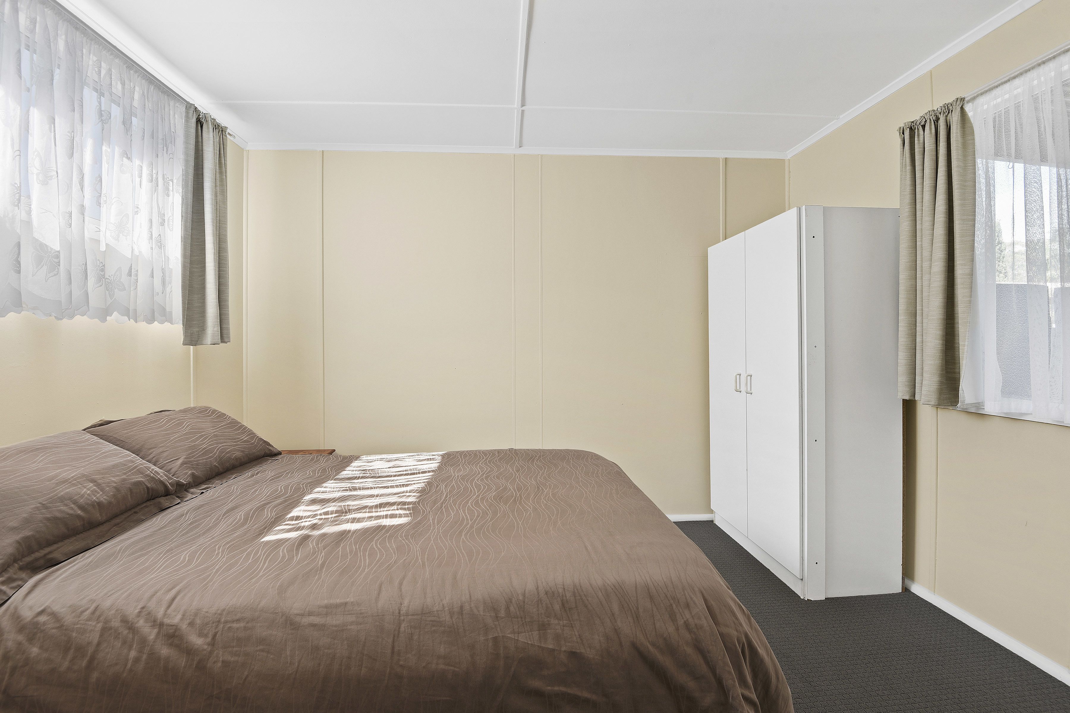 Quarto de hotel com cama, guarda-roupa e janela com cortinas.
