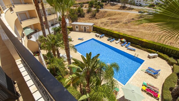 Piscina rodeada por espreguiçadeiras e palmeiras, com vista para edifícios de apartamentos ao fundo.